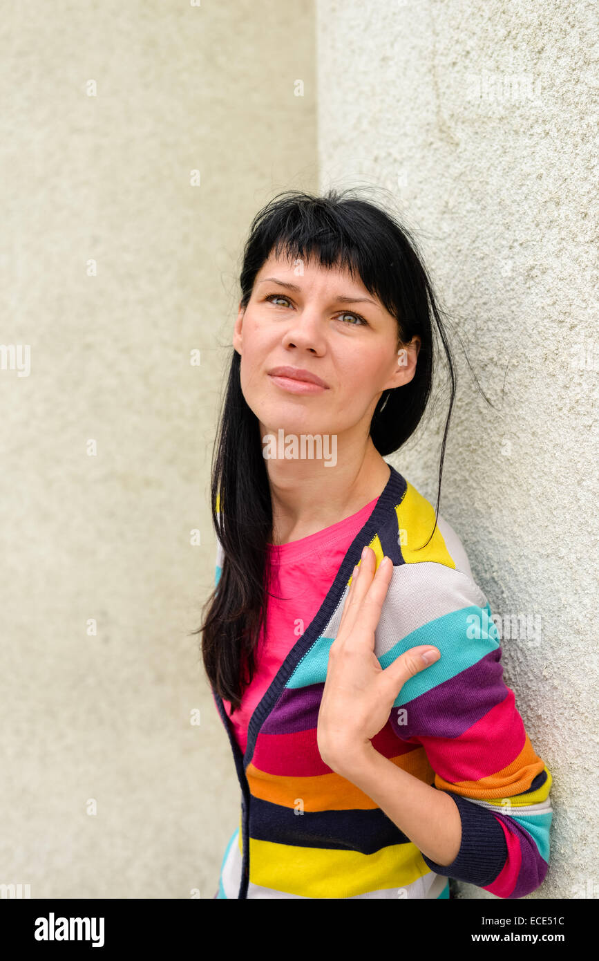 Girl stands leaning against a white wall with one hand on his shoulder ...