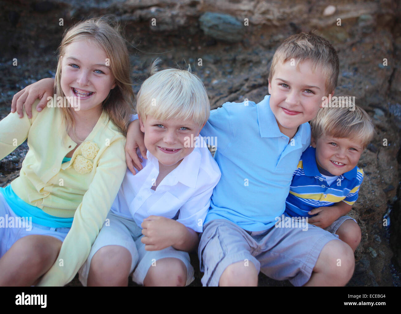 Four children sitting on rocks hugging Stock Photo - Alamy