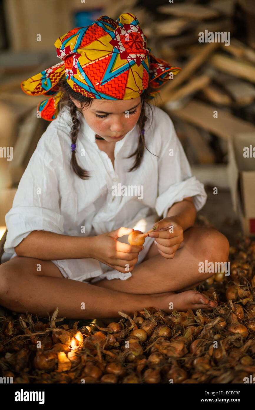 Portrait of girl sitting on pile of onions holding onion bulb Stock ...