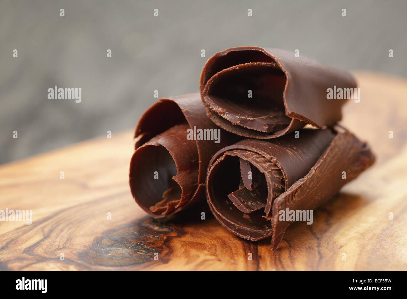 three peeled chocolate curls on olive wood board, closeup photo Stock ...