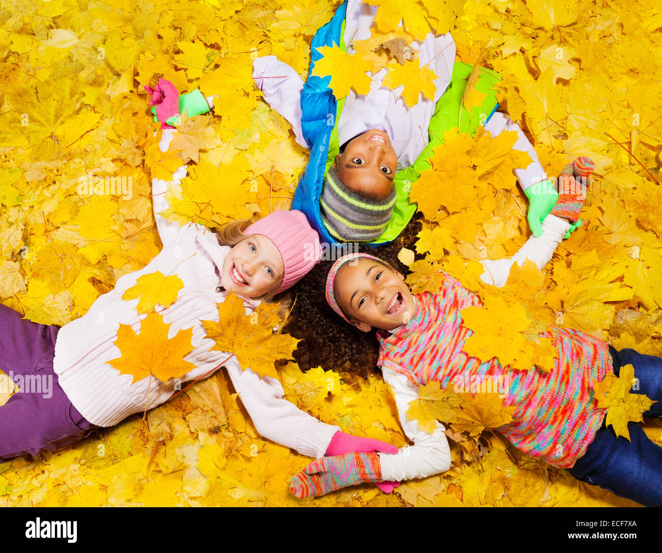 Three kids, girls and a boy laying and smiling on the ground covered ...