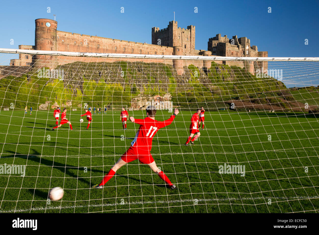 A team palying football infront of Bamburgh Castle, Northumberland, UK ...