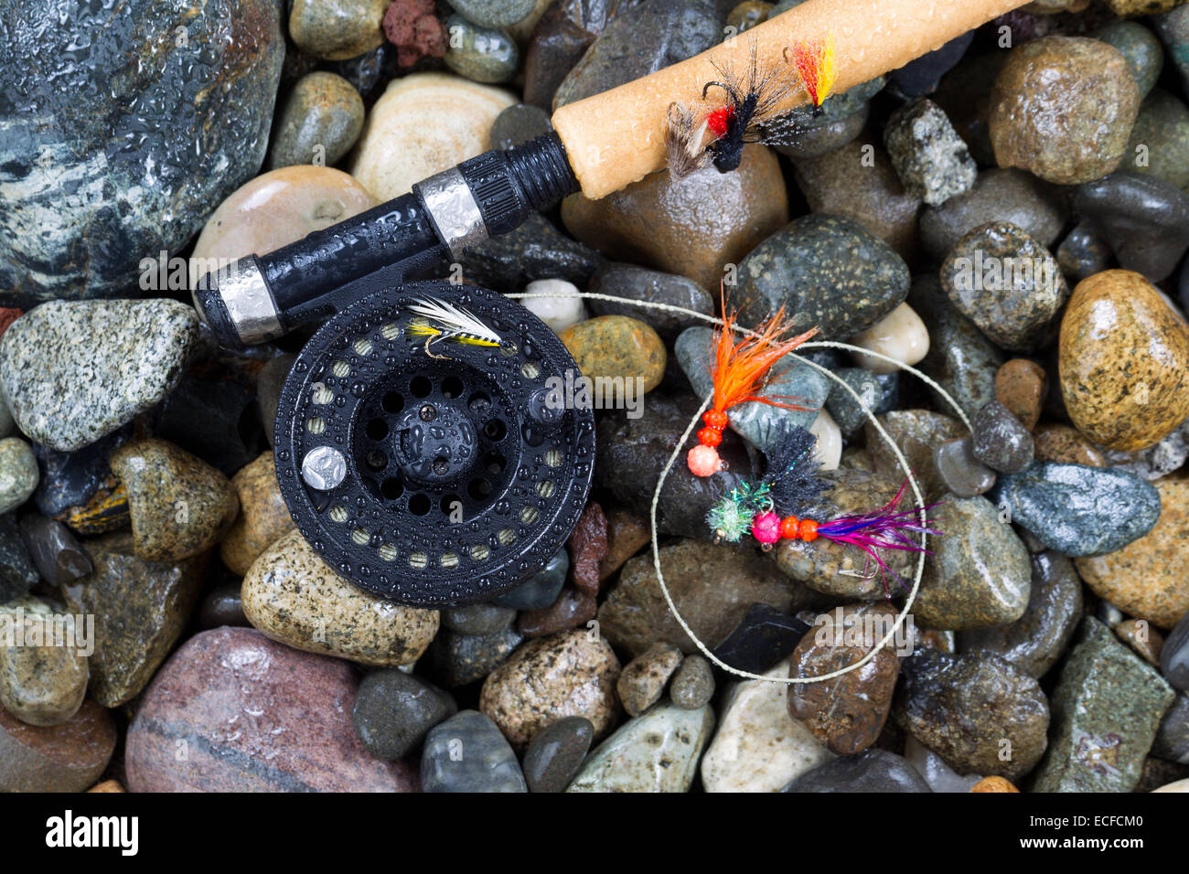 Overhead view of fishing fly reel and assorted flies on wet river bed ...