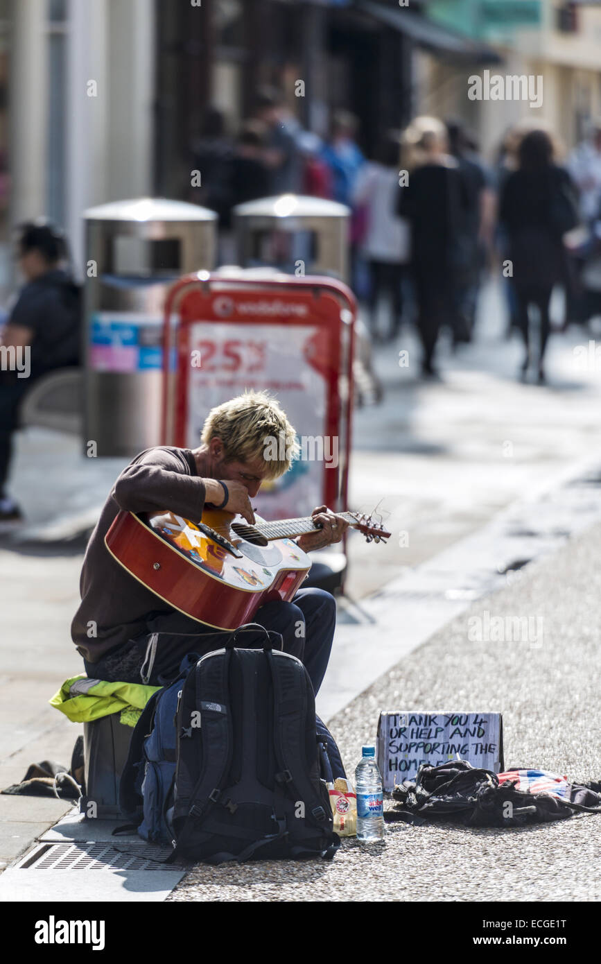 A street musician with a cigarette playing the guitar and a sign saying ...