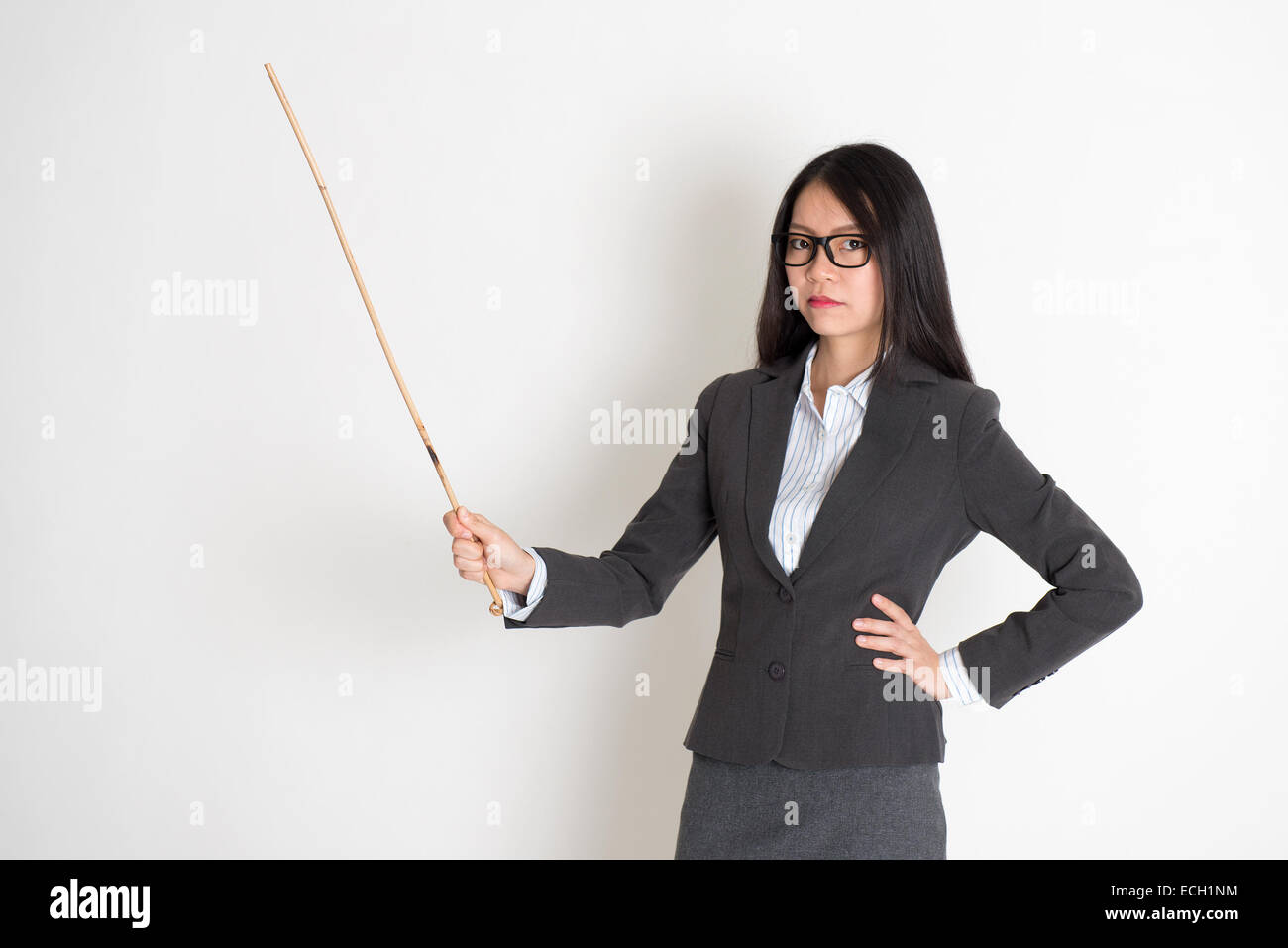Asian female teacher angry and holding a stick, standing on plain ...