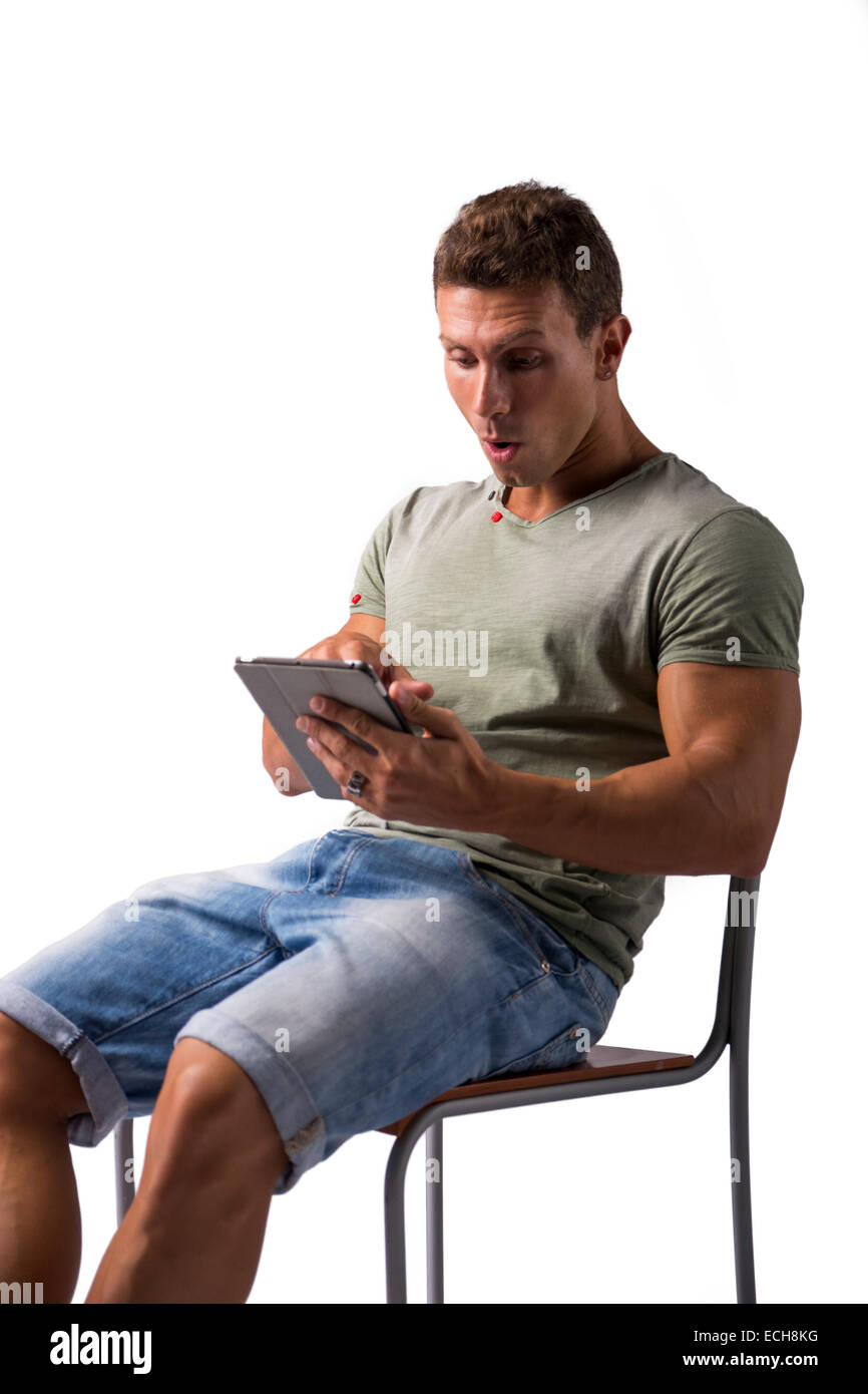 Muscular young man sitting on chair while reading from e-book device ...