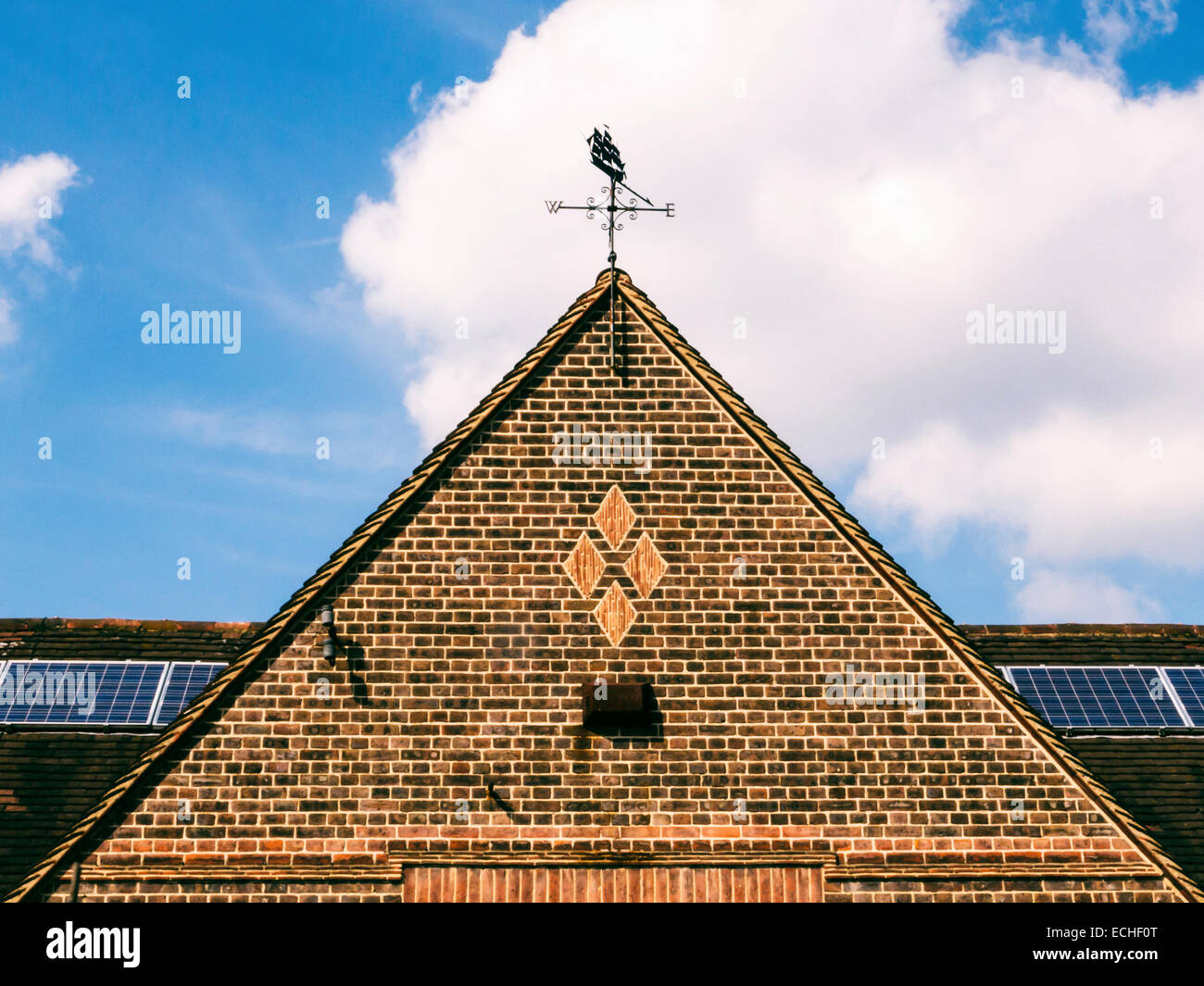 Ship weather vane on brick gable and solar panels on roof of building ...