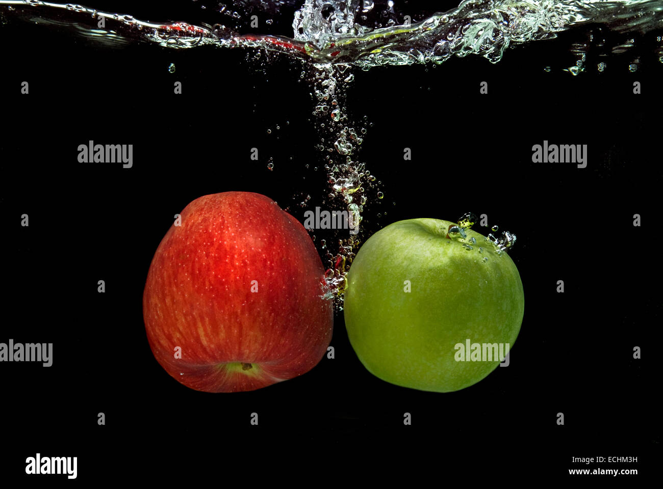 ref and green apple dropped into water with splash isolated on black ...