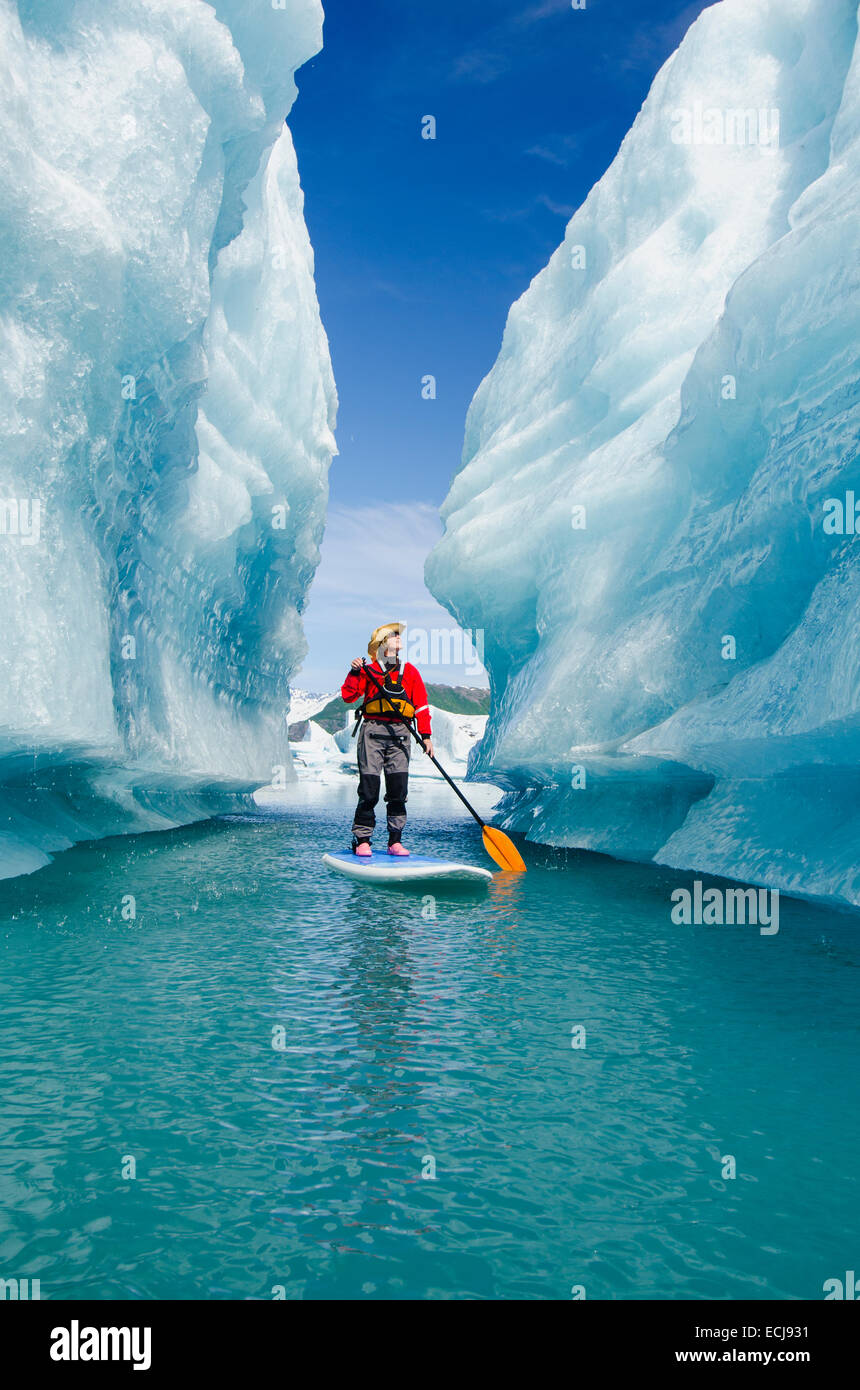 A woman on stand up paddle board (SUP) explores an iceberg canyon on ...