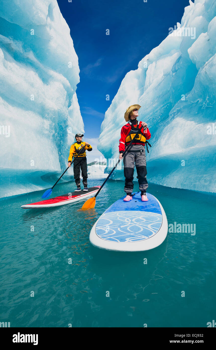 A couple on stand up paddle boards (SUP) explore an iceberg canyon on ...