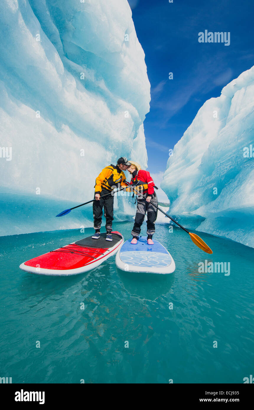 A couple on stand up paddle boards (SUP) kiss in an iceberg canyon on ...