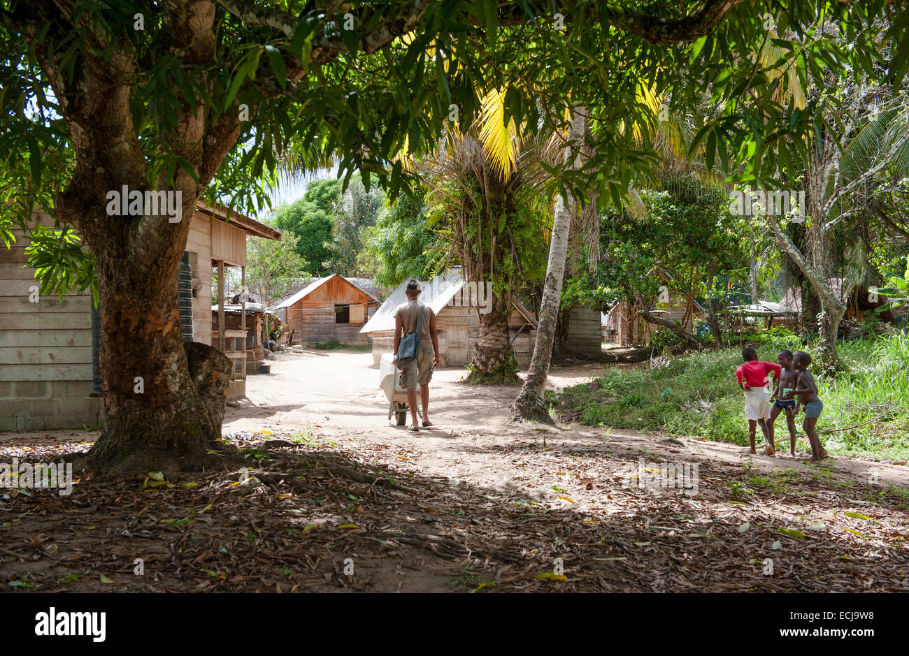 Man pushing wheel cart along traditional wooden huts with palm roofs at ...