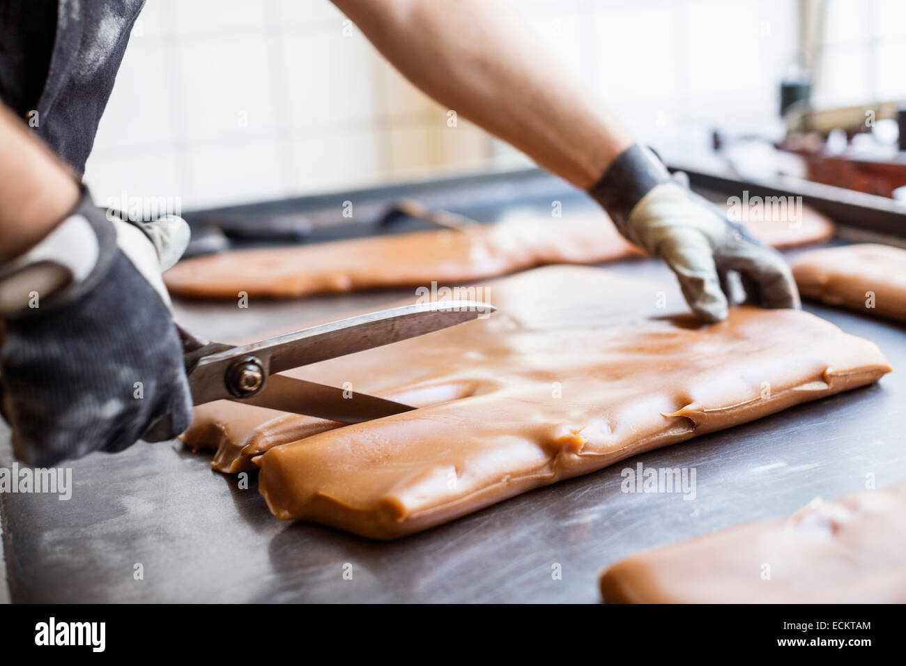 Cropped image of worker cutting caramel with scissors in candy store ...