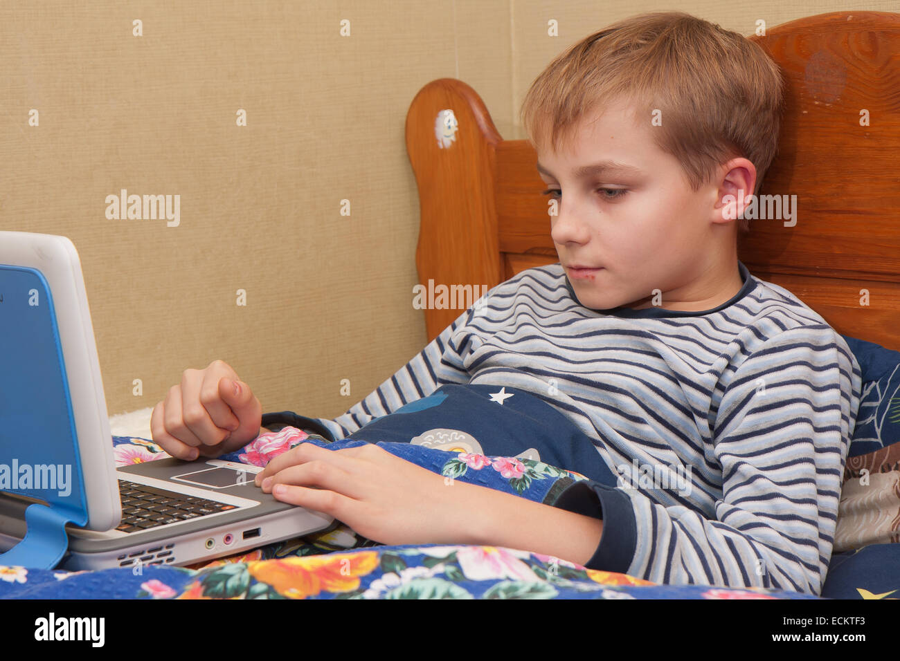 A blond hair boy is playing computers games on a laptop while lying in ...