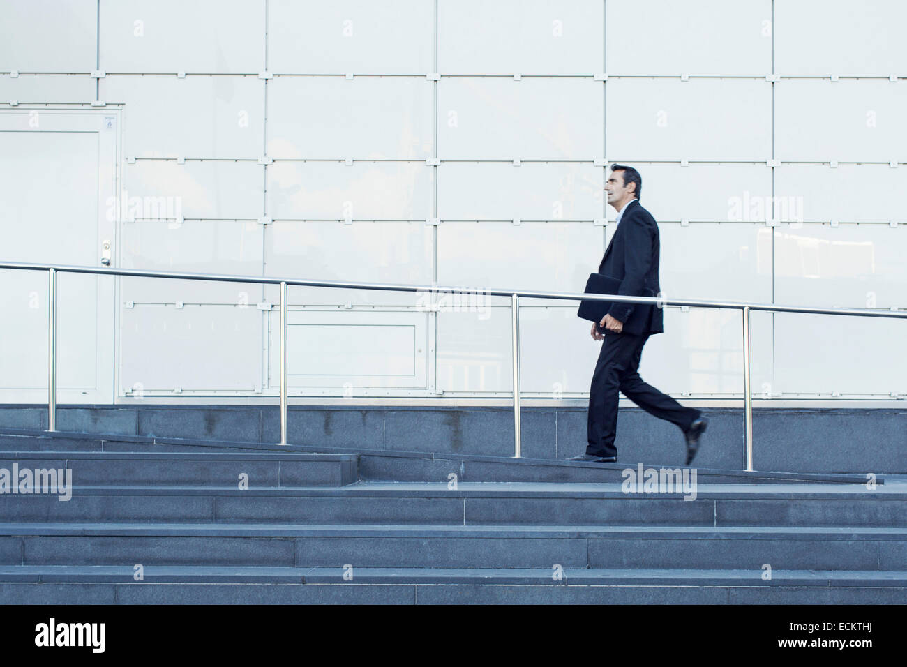 Side view of businessman walking by railing outside office building ...