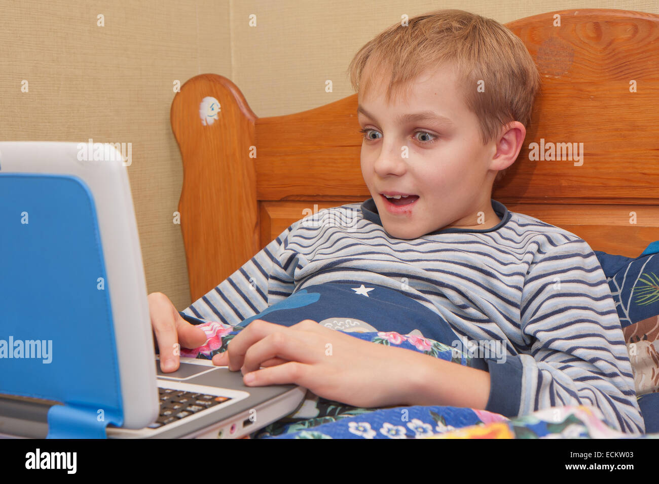 A blond hair boy is playing computers games on a laptop while lying in ...