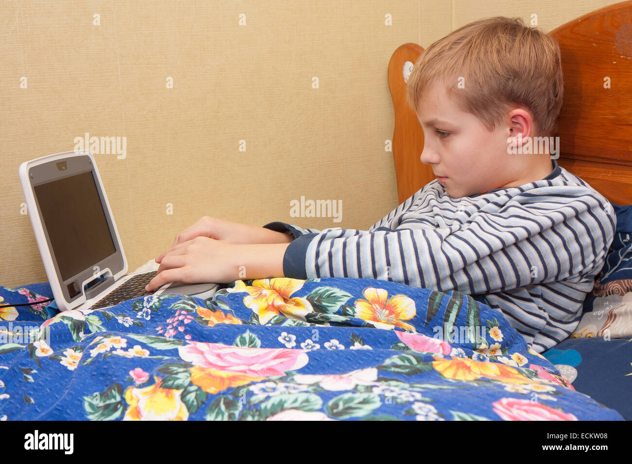 A blond hair boy is playing computers games on a laptop while lying in ...