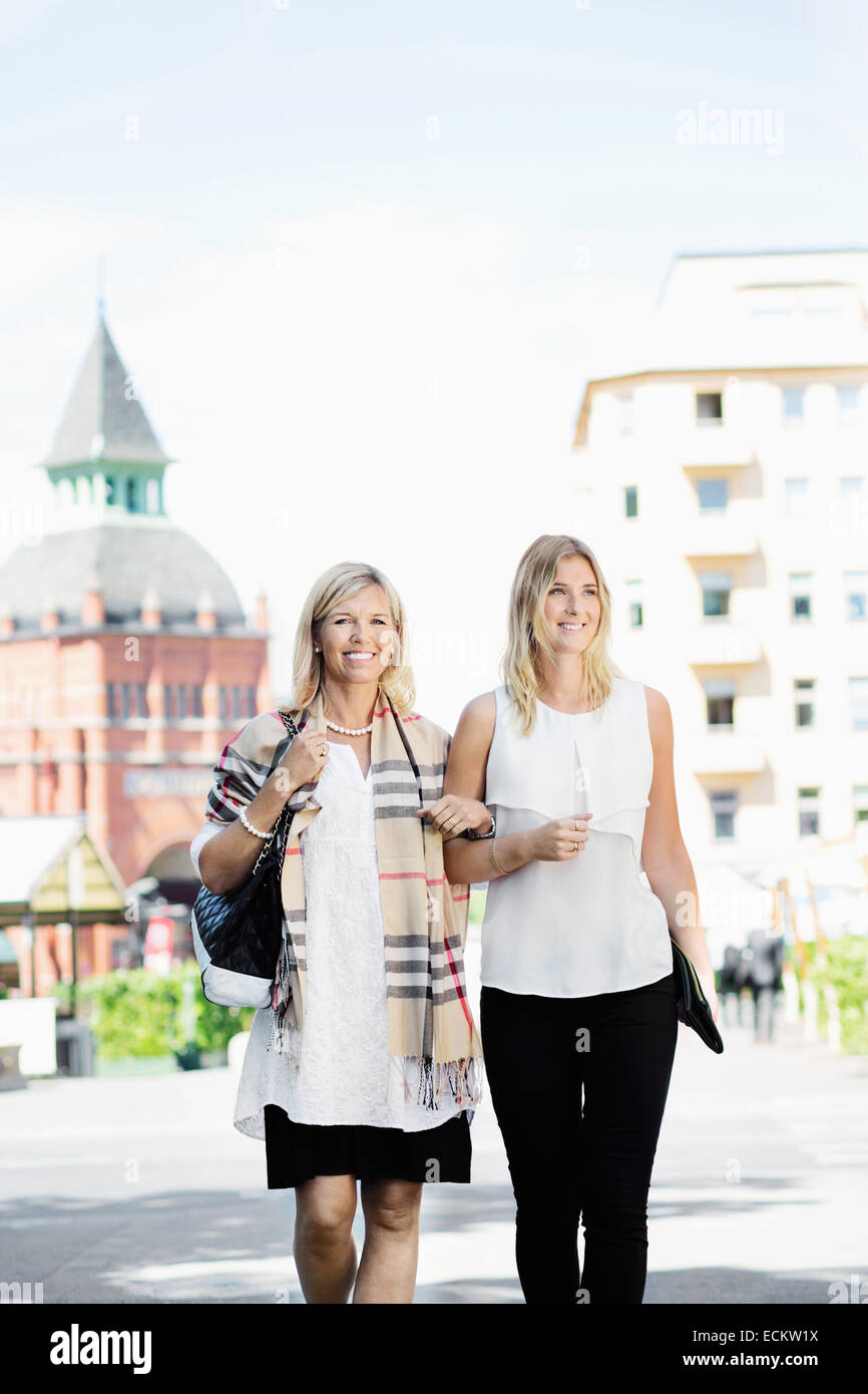 Smiling female friends walking with arm in arm on city street Stock ...