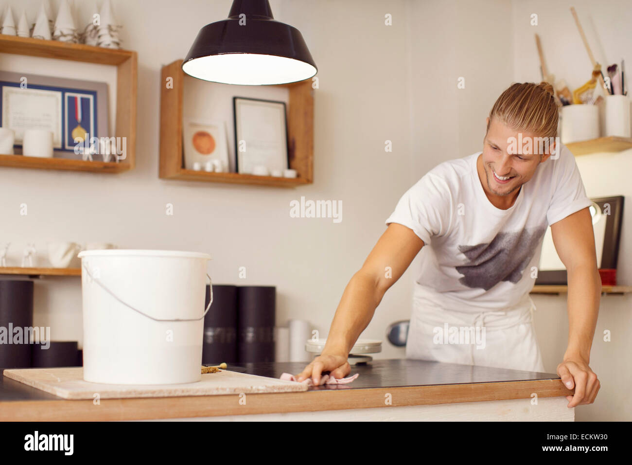 Smiling male worker cleaning table in crockery workshop Stock Photo - Alamy