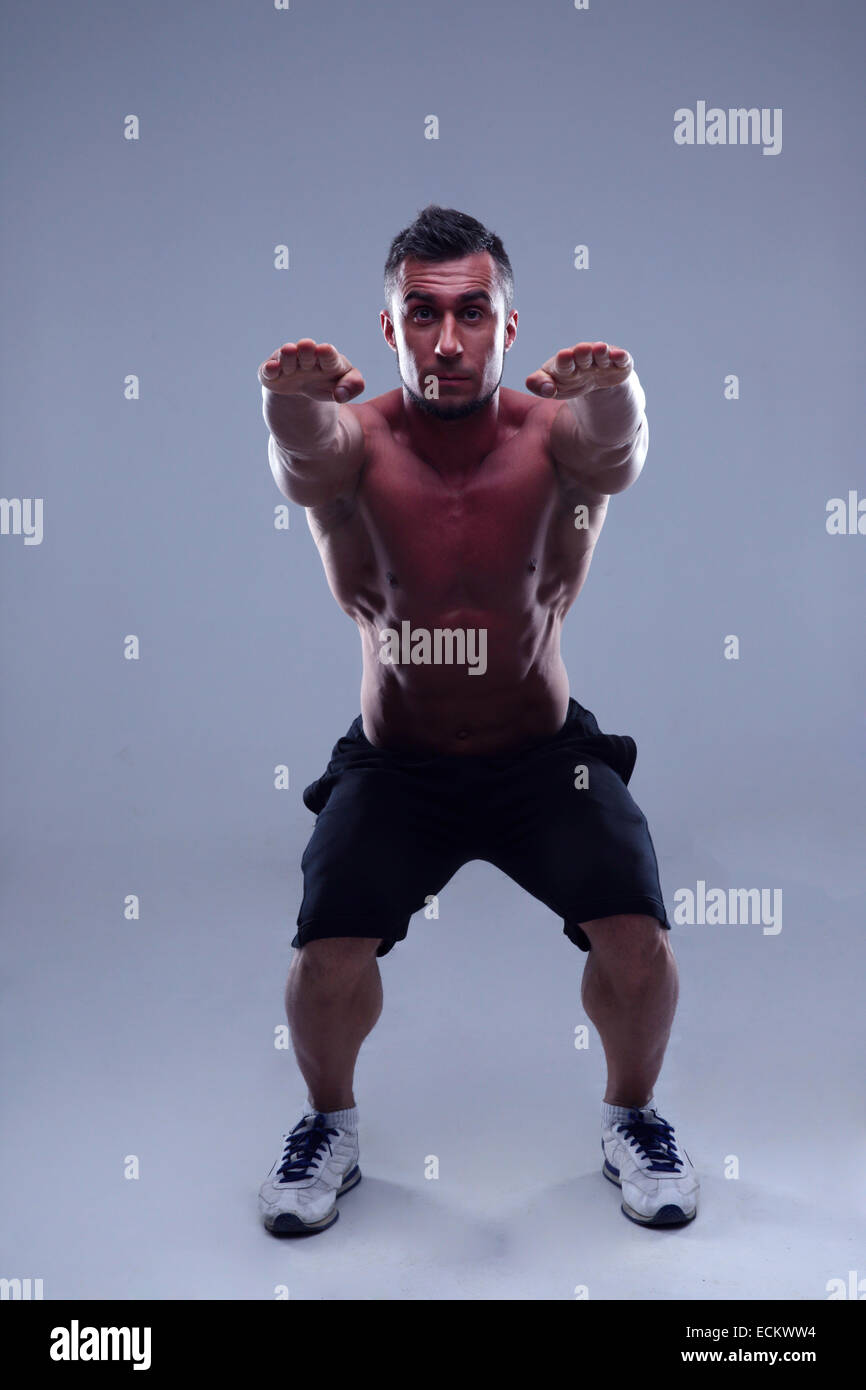 Muscular handsome man doing squats over gray background Stock Photo - Alamy