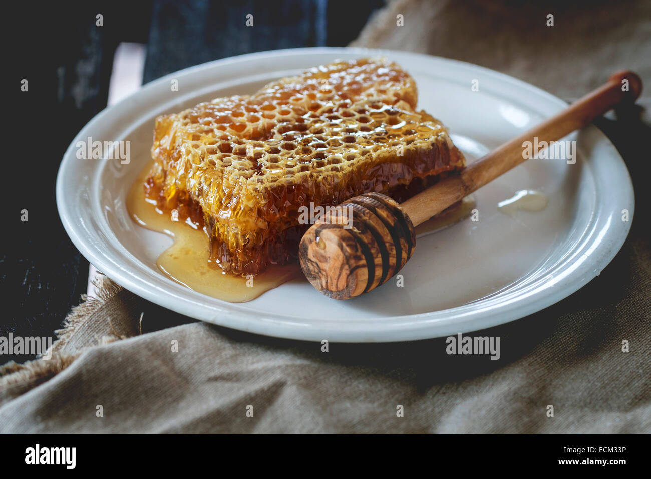 Honeycomb with honey dipper on ceramic plate over old wooden table ...