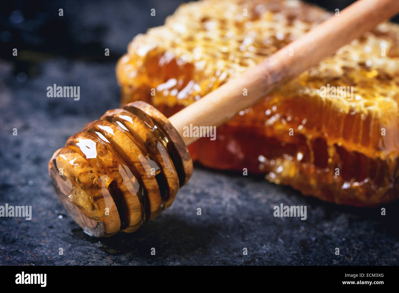 Honeycomb with honey dipper over black surface Stock Photo - Alamy