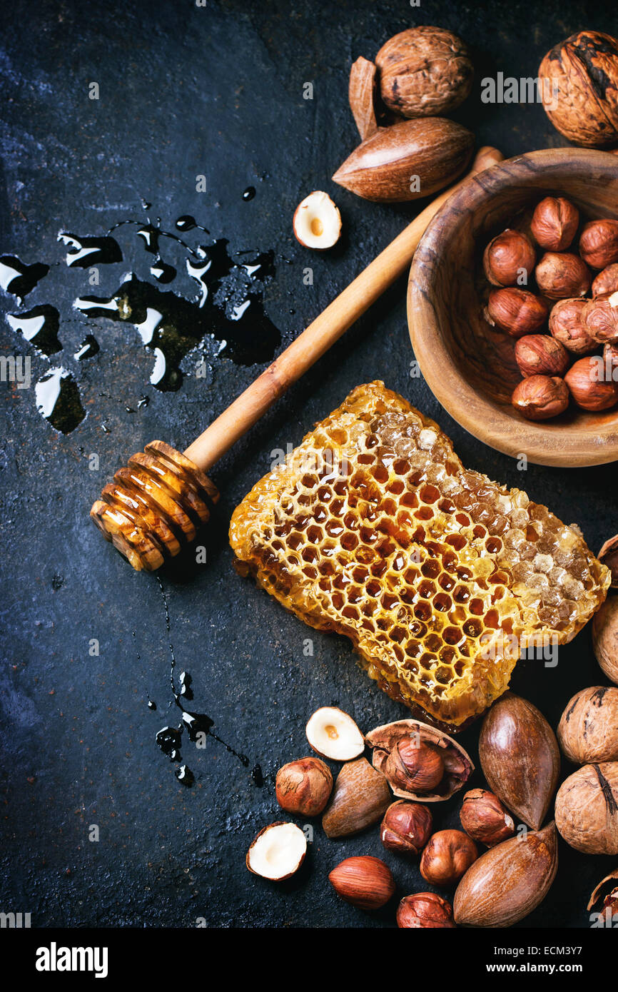 Honeycomb with honey dipper and mix of nuts over black surface. Top ...