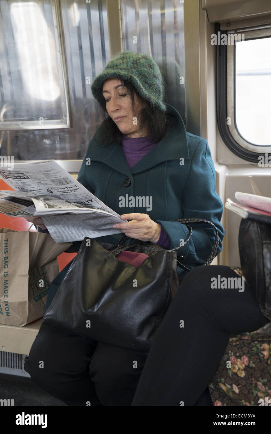Woman reads a paper while riding a subway train in Brooklyn, NY Stock ...