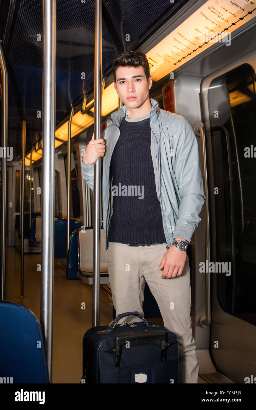 Young man standing in subway train going on vacation with trolley ...