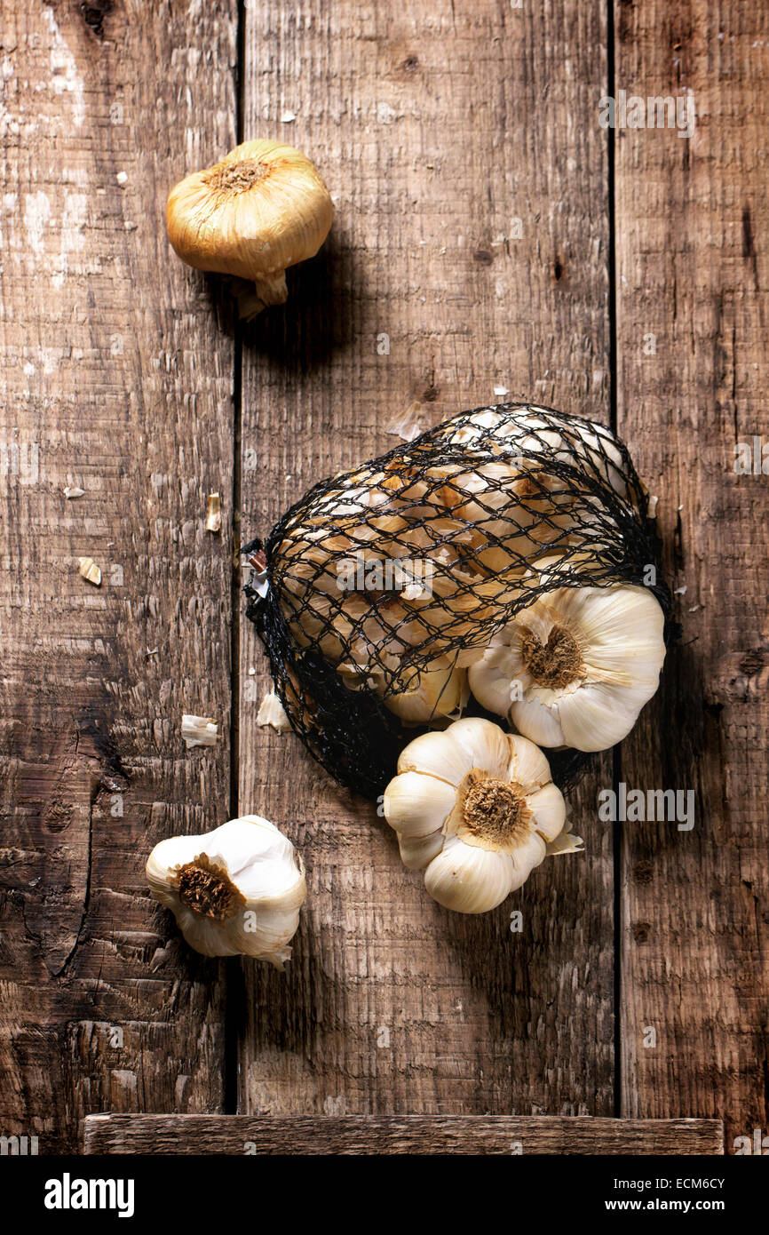 Mesh bag of smoked garlic over wooden background. Top view. See series ...