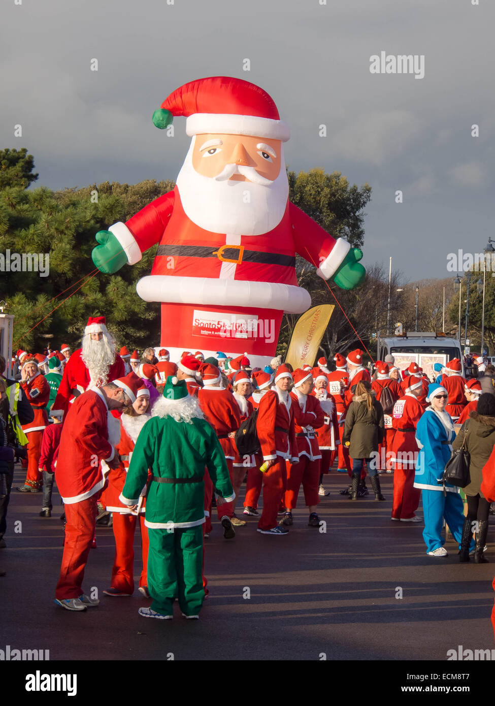 Runners dressed as Santa Clause stand in front of an inflatable Santa ...