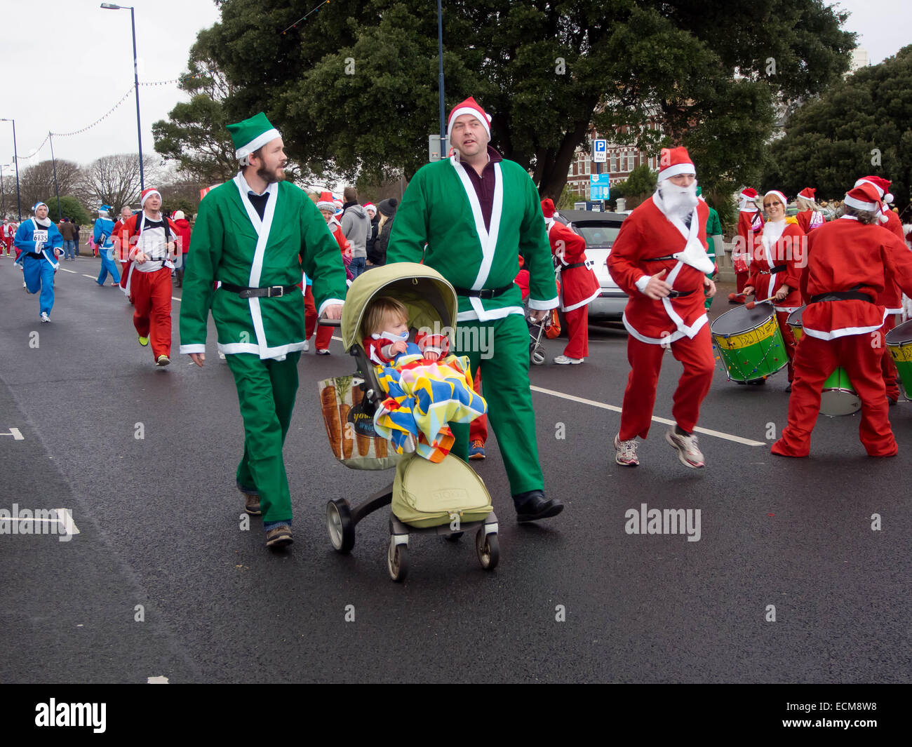 Two male Participants dressed as Santa Clause push a toddler in a push ...