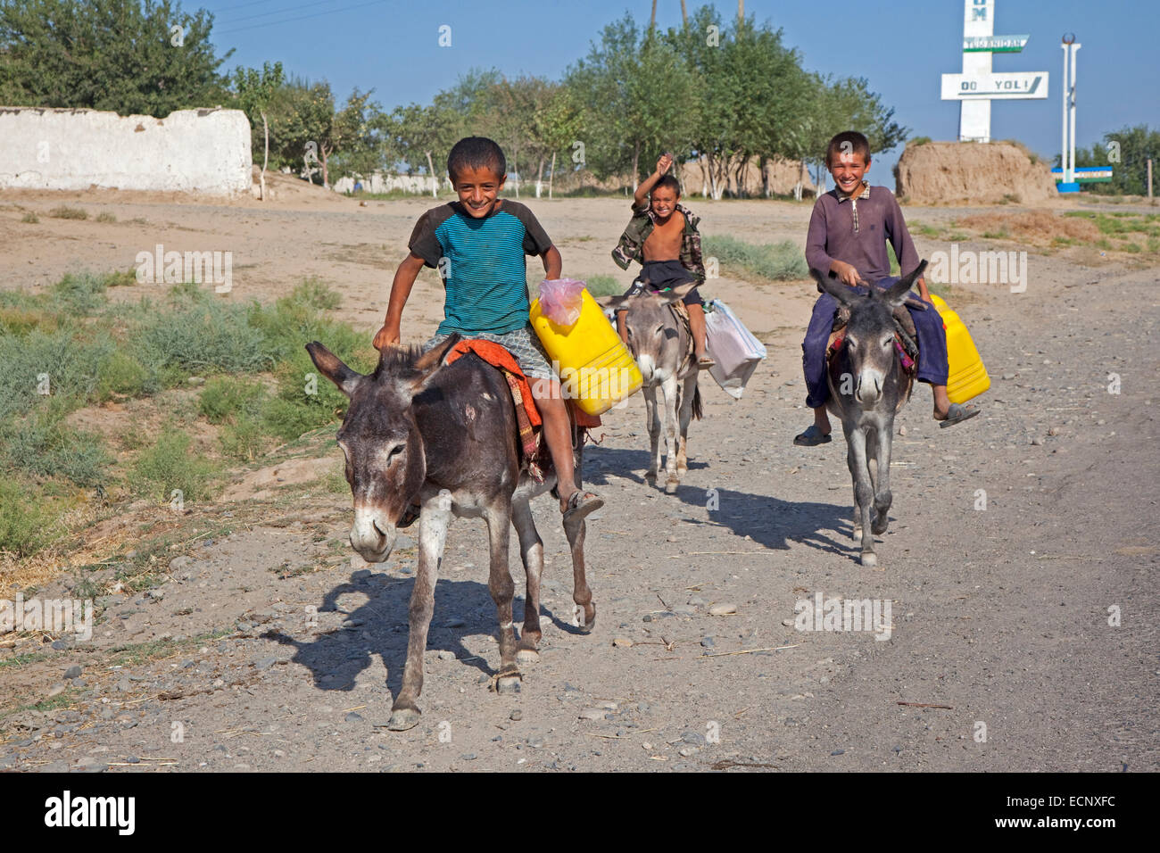 Three children riding donkeys with plastic containers to collect water ...