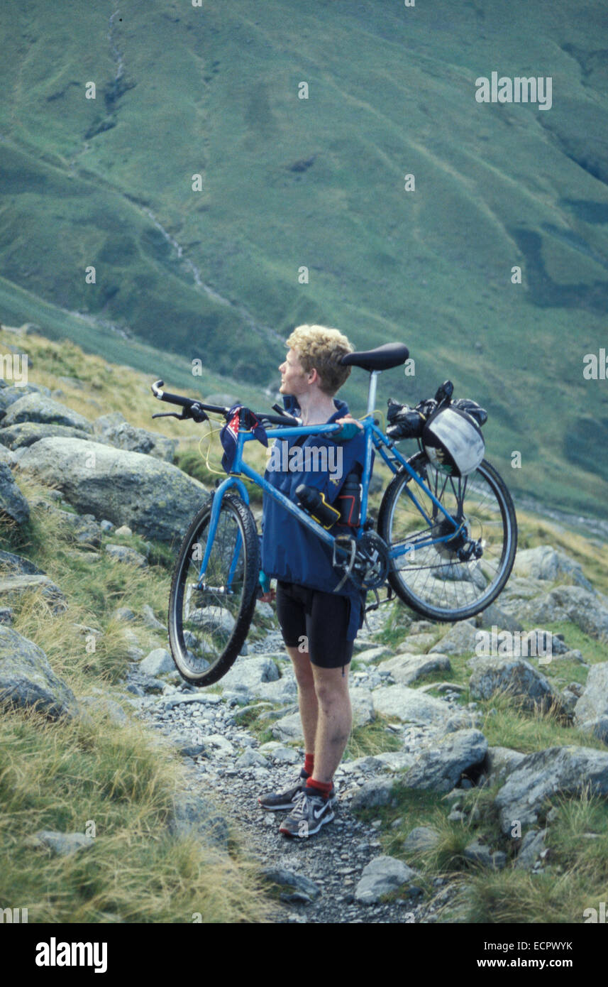 A cyclist carrying his bike on the track to Stake Pass behind Langdale ...