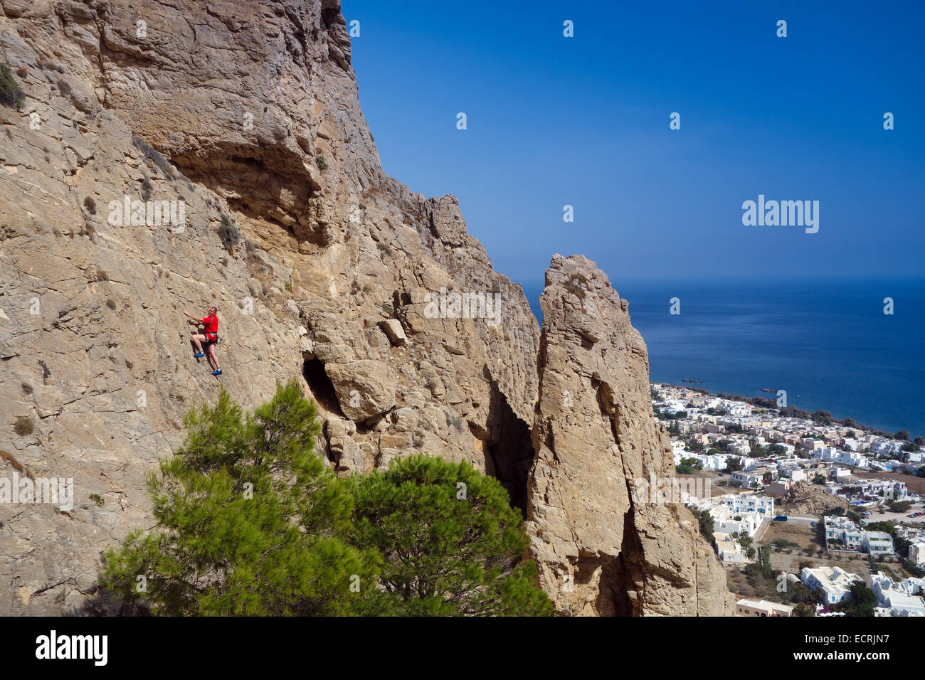 Male rock climber in shorts and red shirt on smooth cliff above white ...