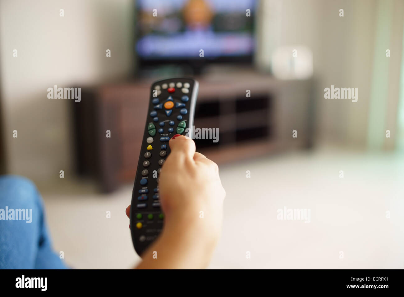 Over the shoulder view of girl sitting on sofa holding tv remote and ...