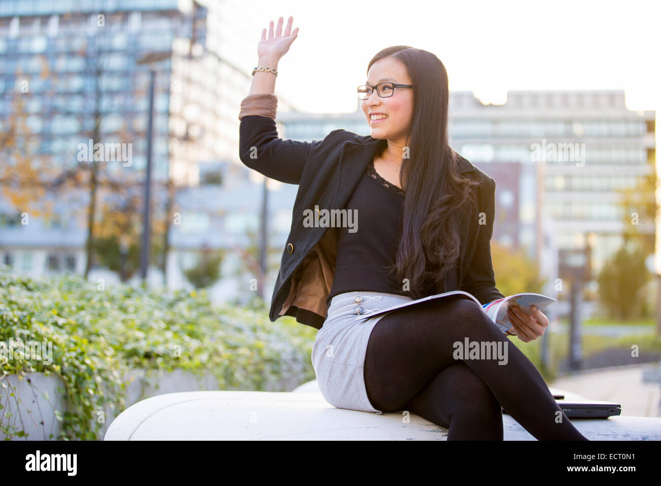 Young businesswoman with magazine greeting someone Stock Photo - Alamy