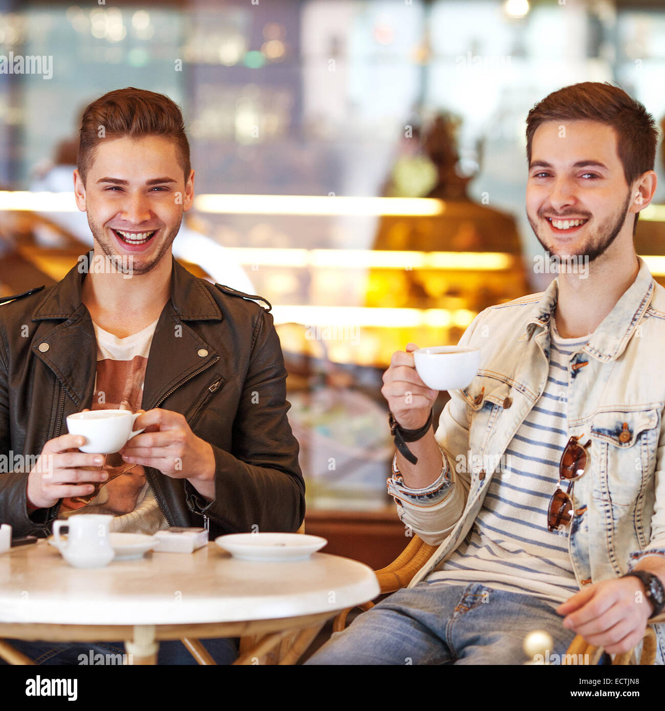 Two young hipster guy sitting in a cafe chatting and drinking coffee ...