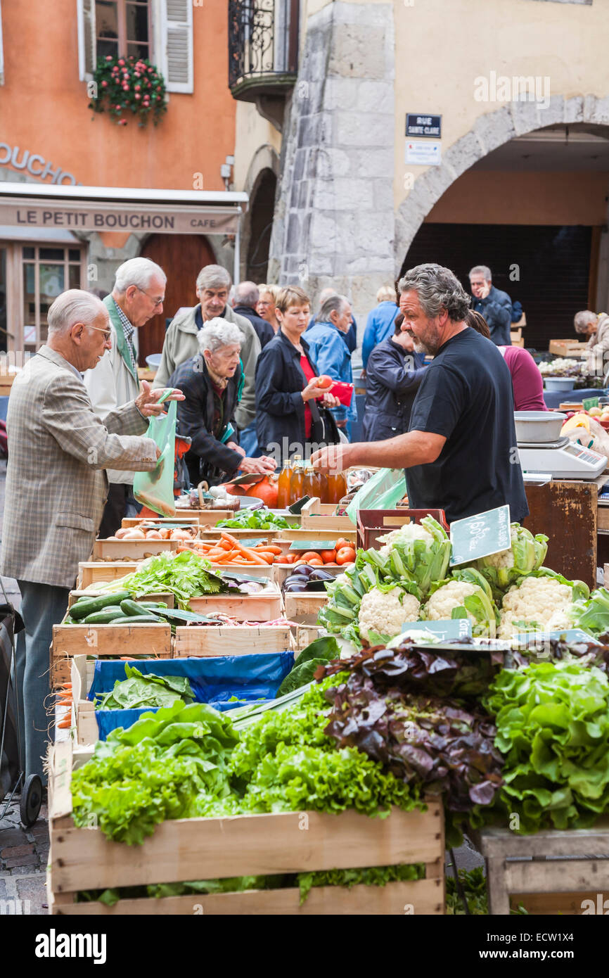 Male French stallholder serving customers at a fresh vegetable and ...