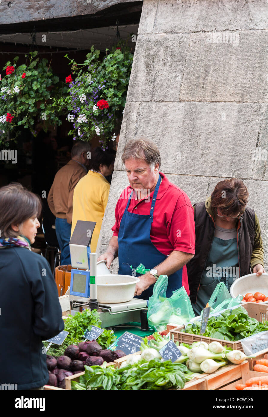 French male stallholder weighing produce and customer at a vegetable ...