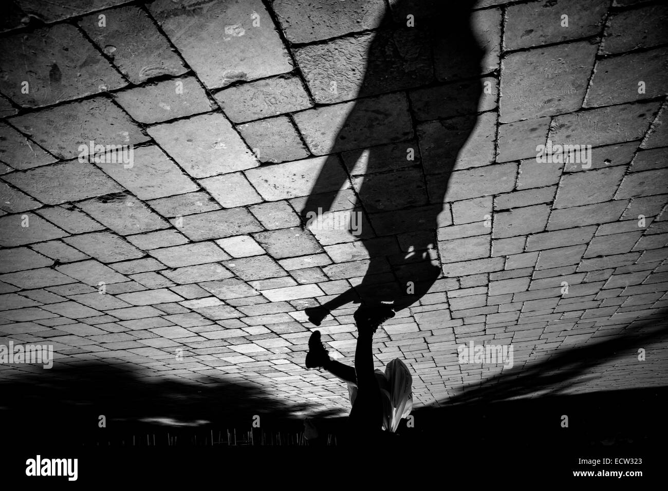 A monochromatic image of the shadow of a person on a stone paved plaza ...