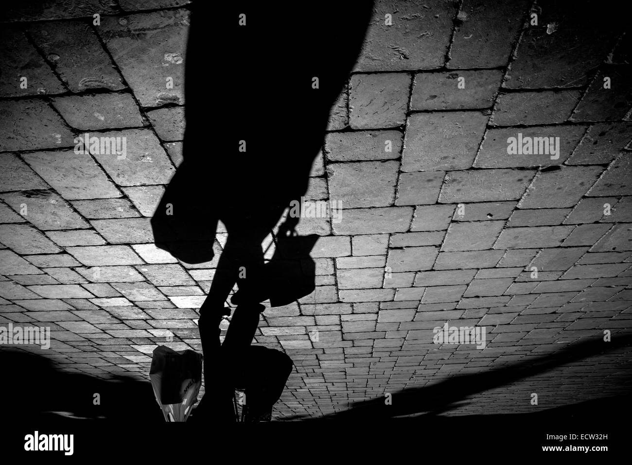 A monochromatic image of the shadow of a person on a stone paved plaza ...
