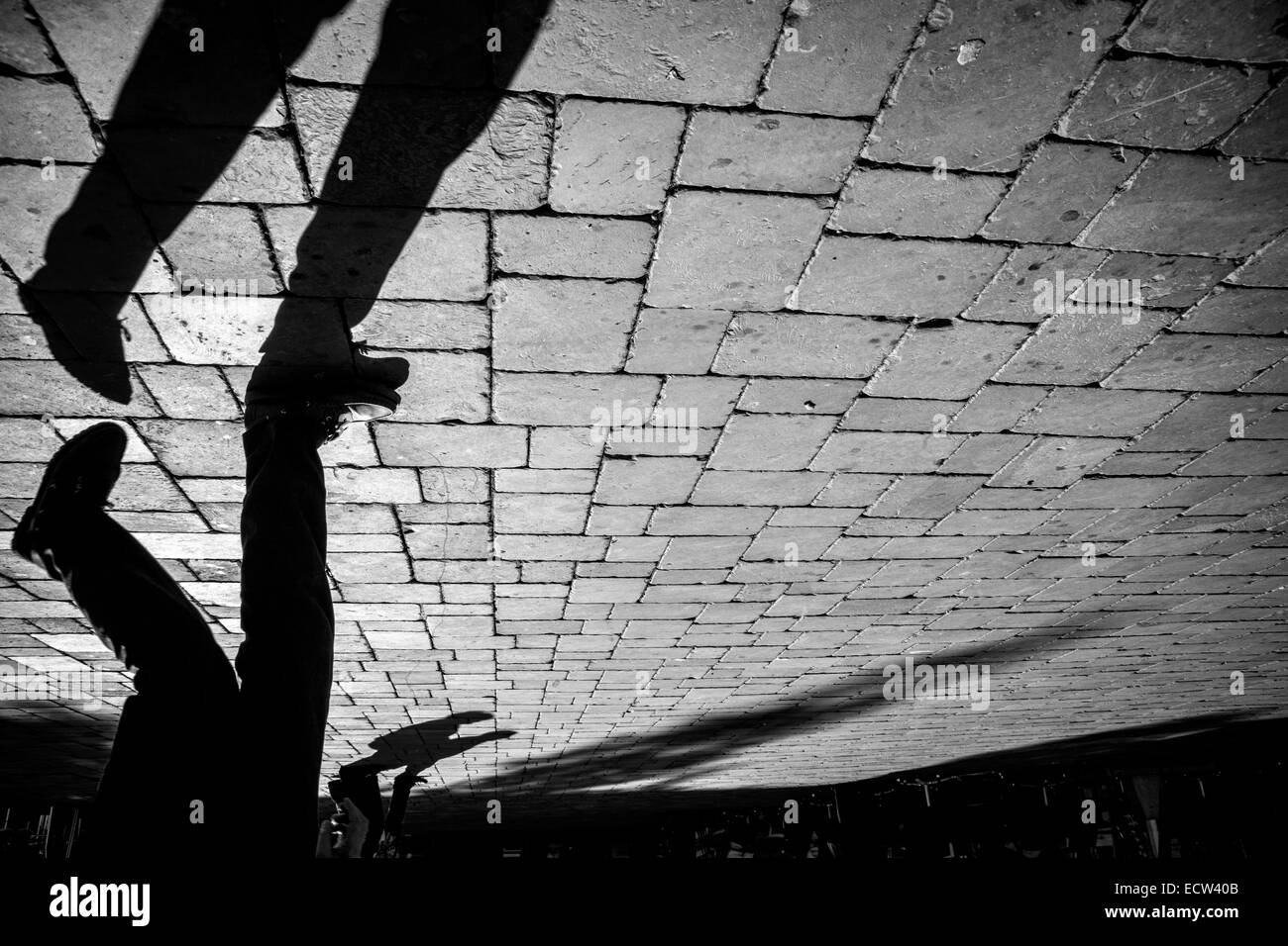 A monochromatic image of the shadow of a person on a stone paved plaza ...