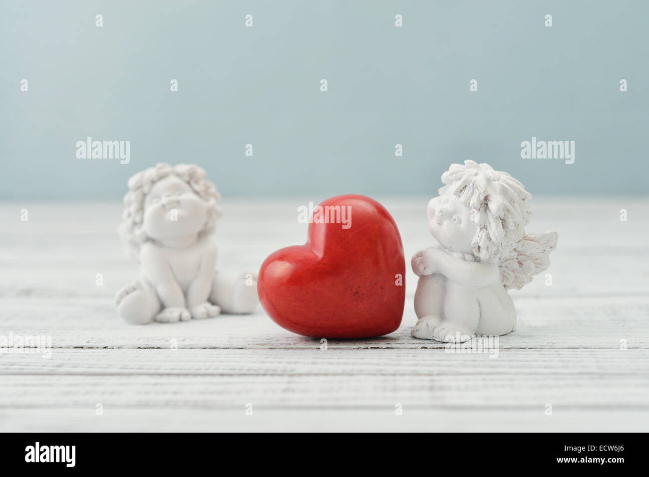 Statuettes of small angels with stone heart over light background Stock ...