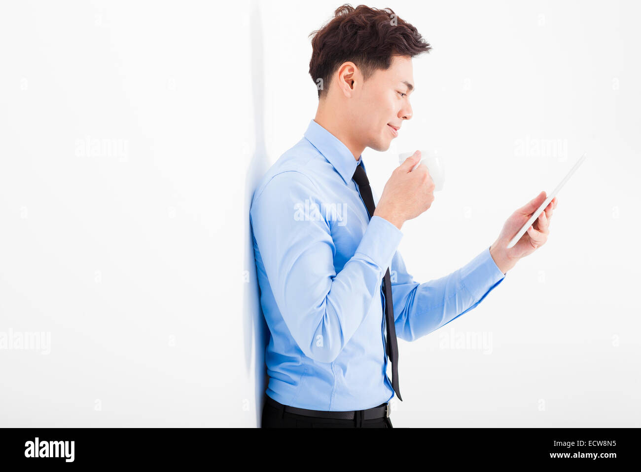 young businessman holding tablet and leaning against white wall Stock ...