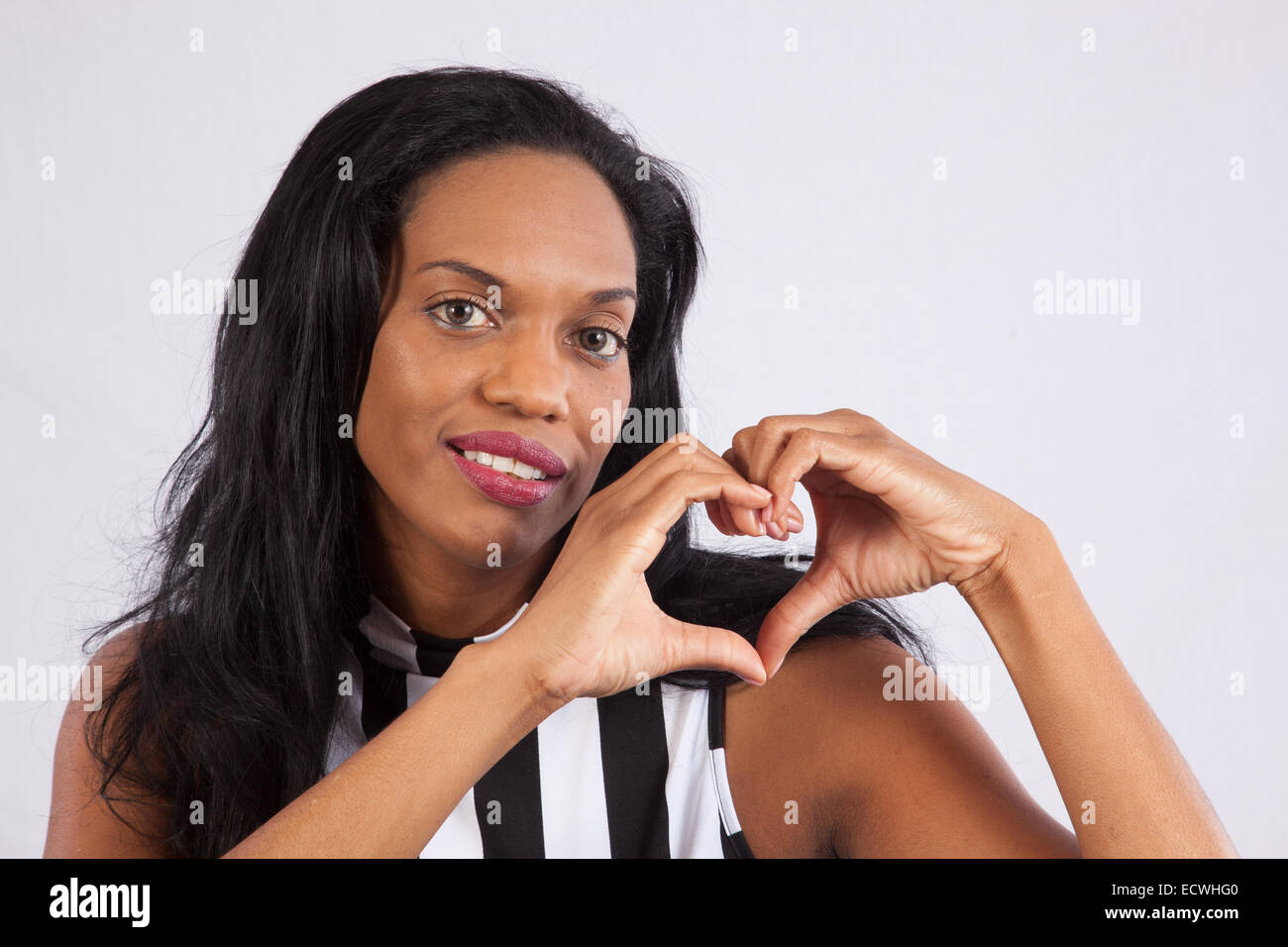 Pretty Black woman sitting with a pleased smile and making a heart with ...