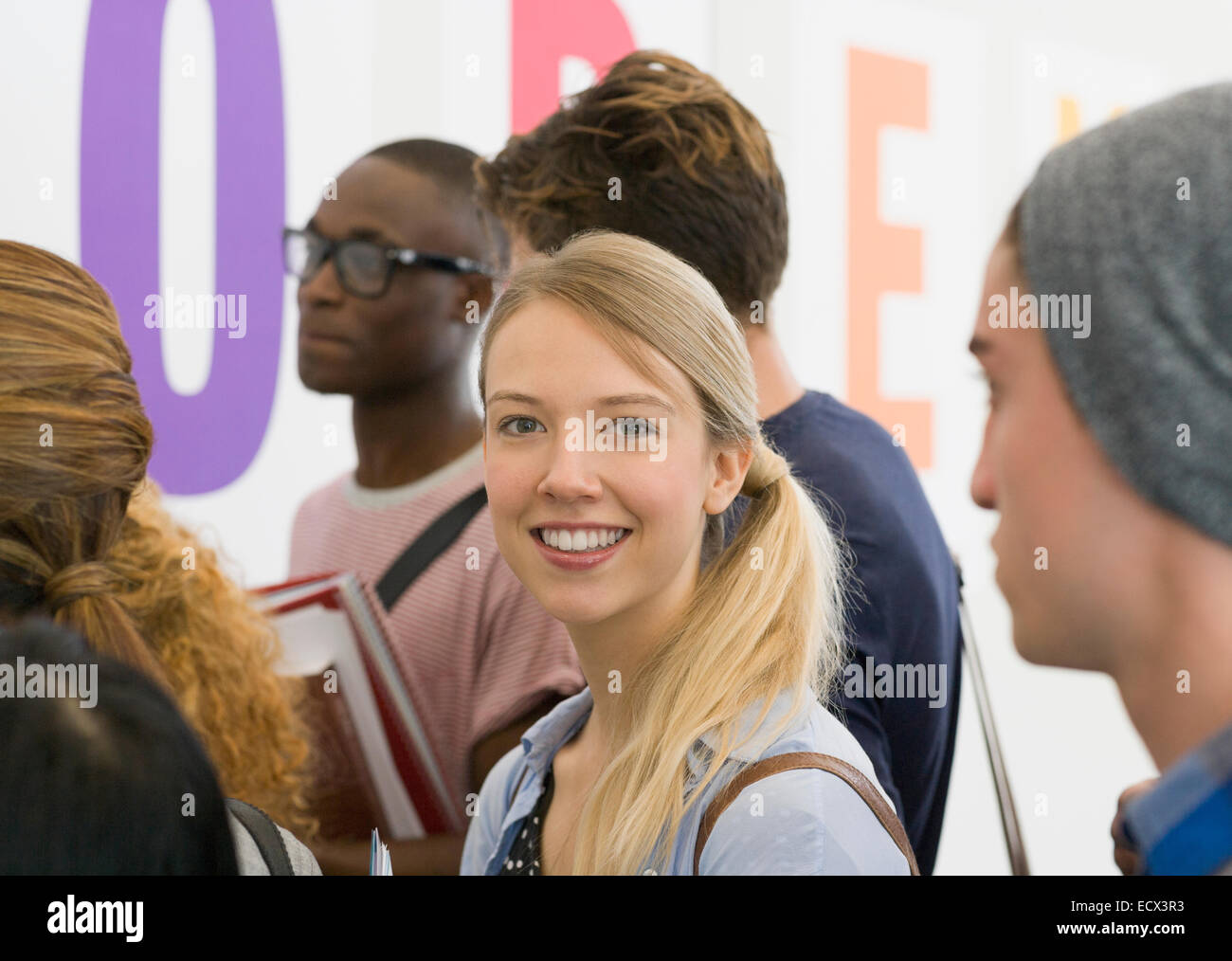 Portrait of university student standing in corridor, students talking ...