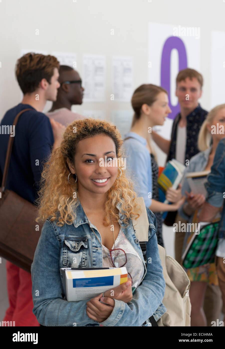 Female student holding books and smiling at camera with group of ...