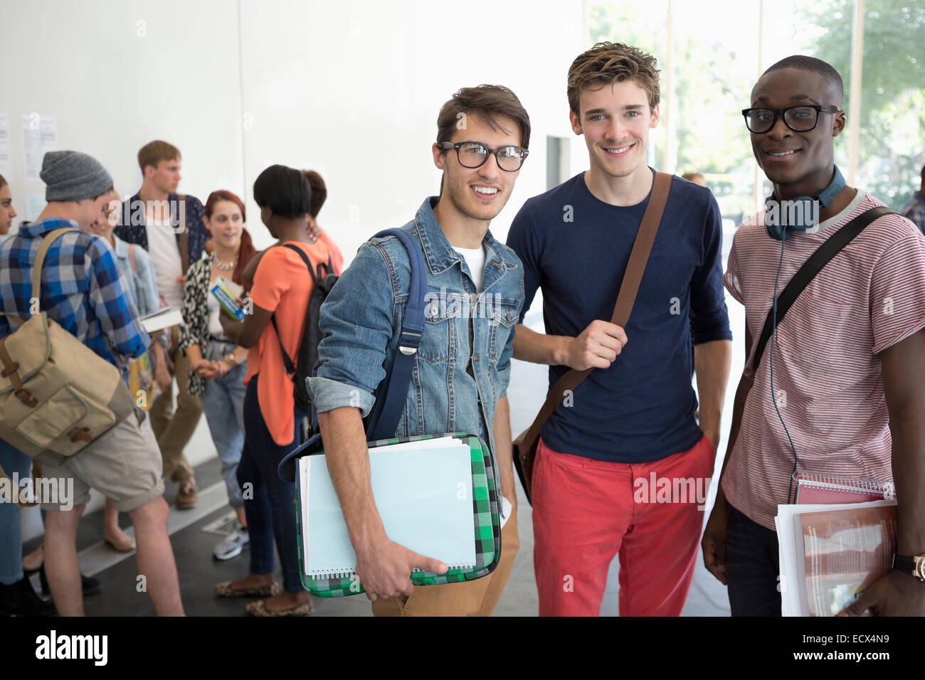 Three smiling male students standing together with other students in ...