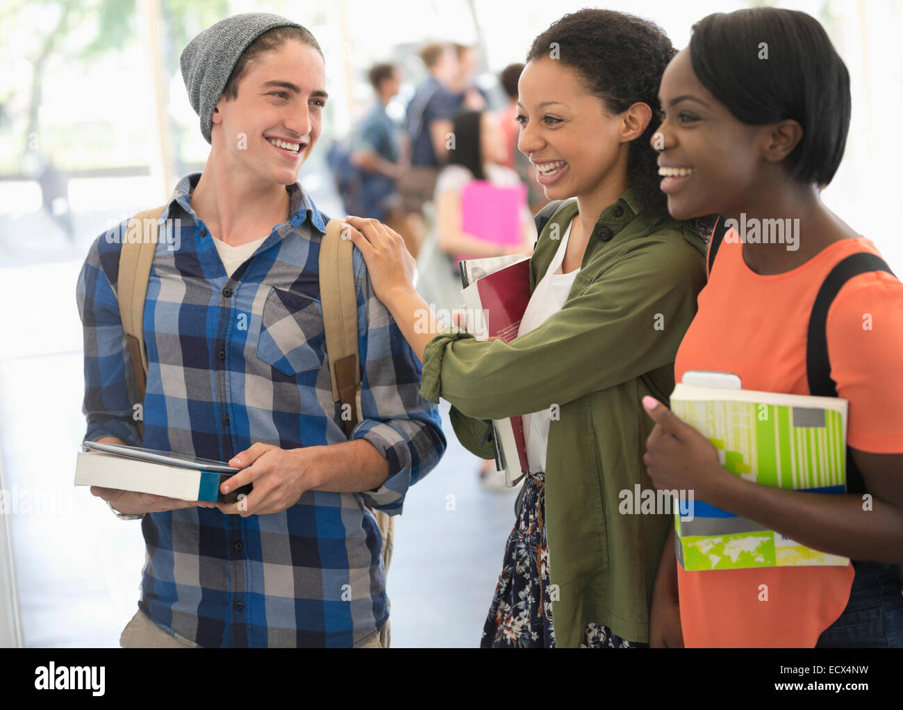 Students holding books and laughing with other students in background ...